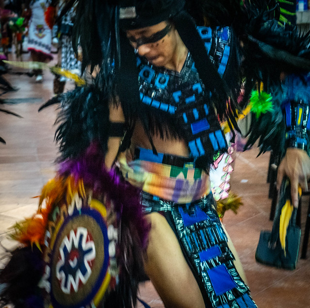 Carnival dancer in a blue sequin costume with black feather accents, mid-movement